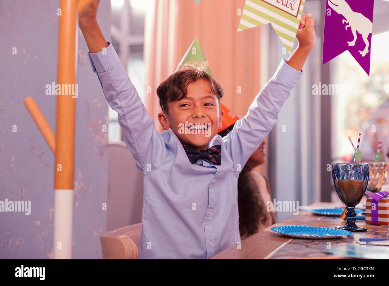 Happy boy sitting at the table and putting hands up at the party Stock ...