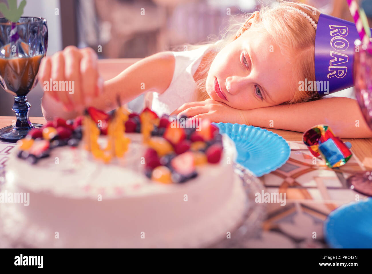 Bored girl leaning on the table and touching candles on her cake Stock ...