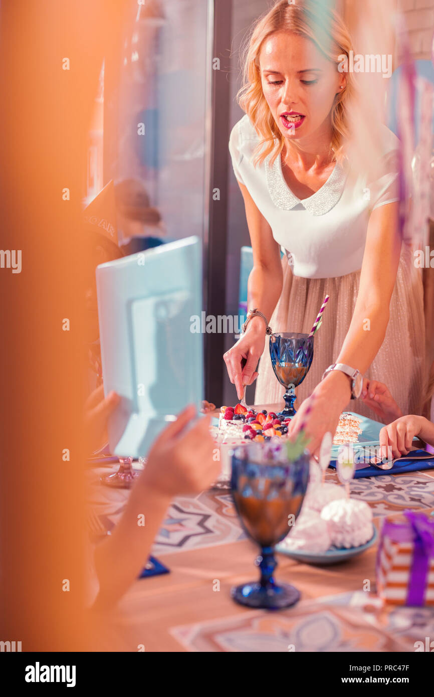 Blonde woman looking concentrated while putting cake for children Stock ...