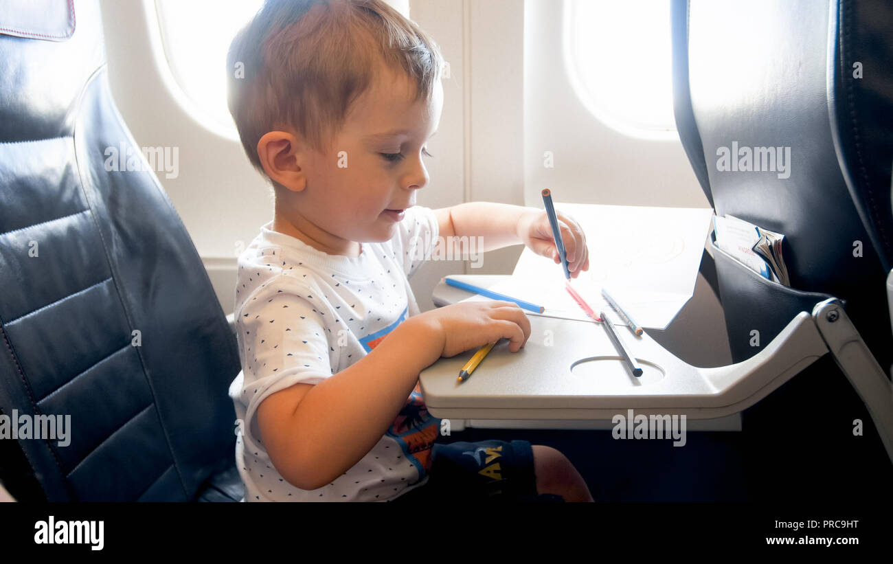 Happy smiling little boy flying in airplane and drawing with pencils ...