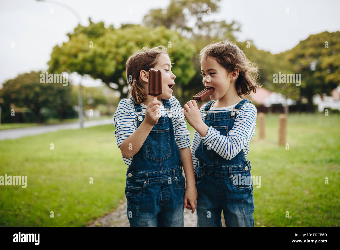 Two little twin sisters in identical clothes standing outdoors and ...