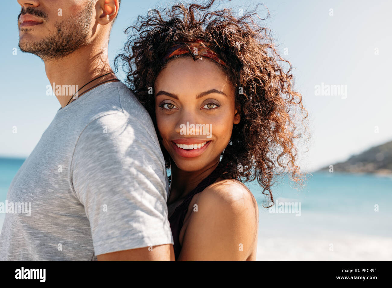 Side view of a smiling woman standing behind her boyfriend hugging him ...
