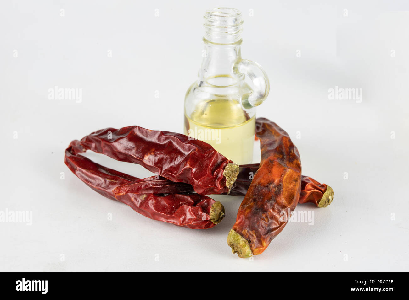 Dried peppers and a vial of oil on a white kitchen table. Spices ...
