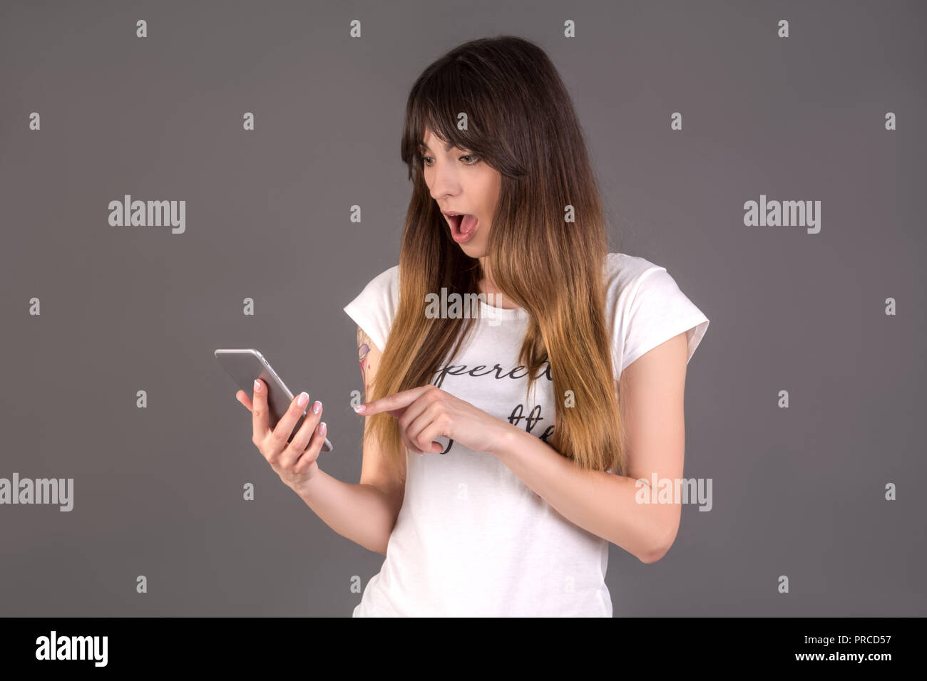 Shocked girl with mobile phone on gray background Stock Photo - Alamy