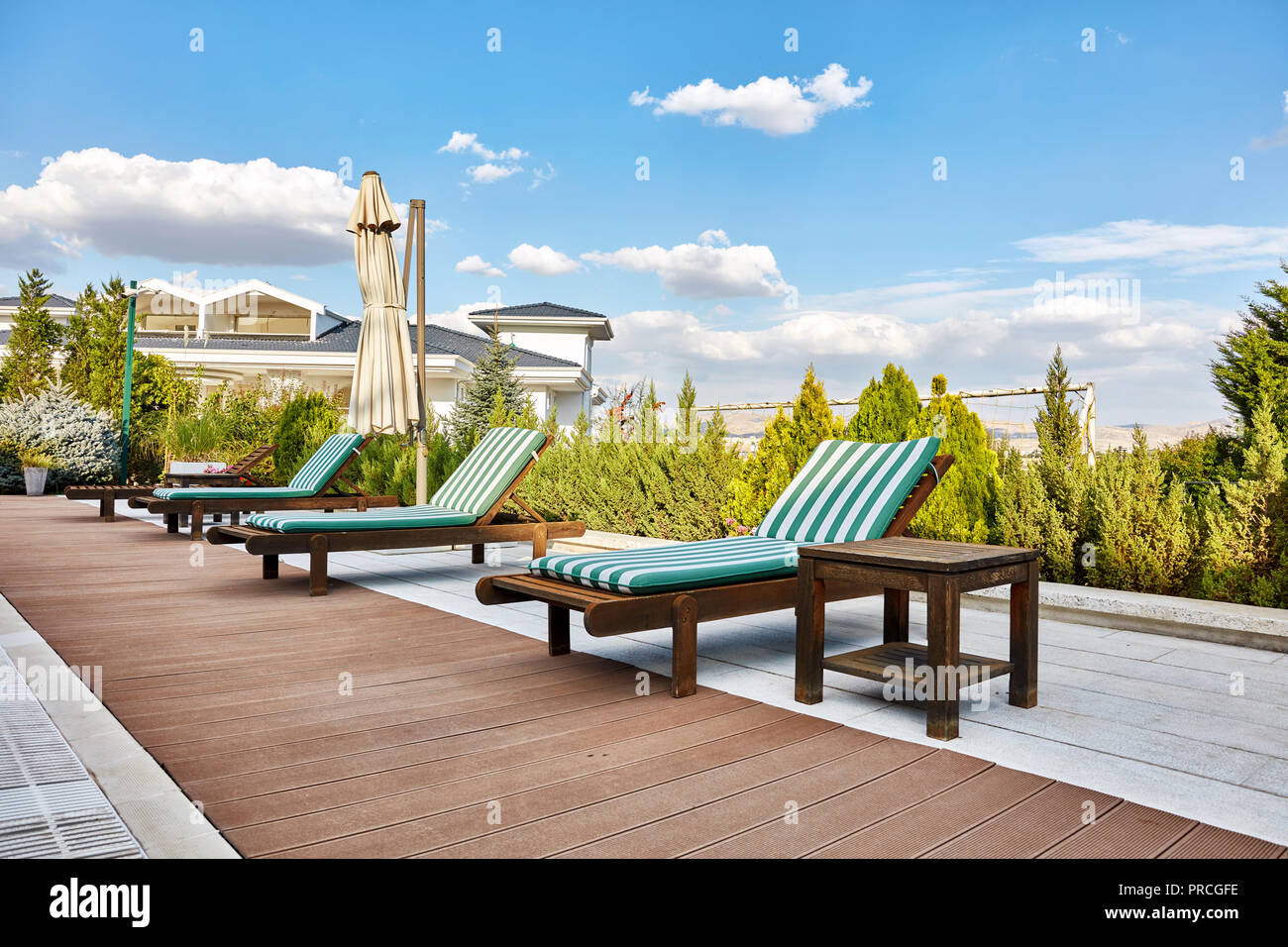 Wooden sunbed deck chairs near an outdoor poolside under diffused ...