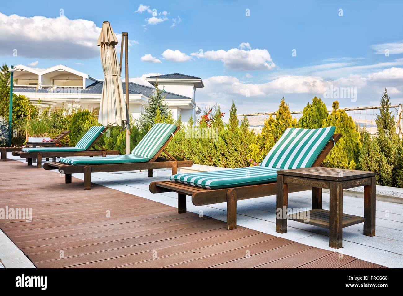 Wooden sunbed deck chairs near an outdoor poolside under diffused ...