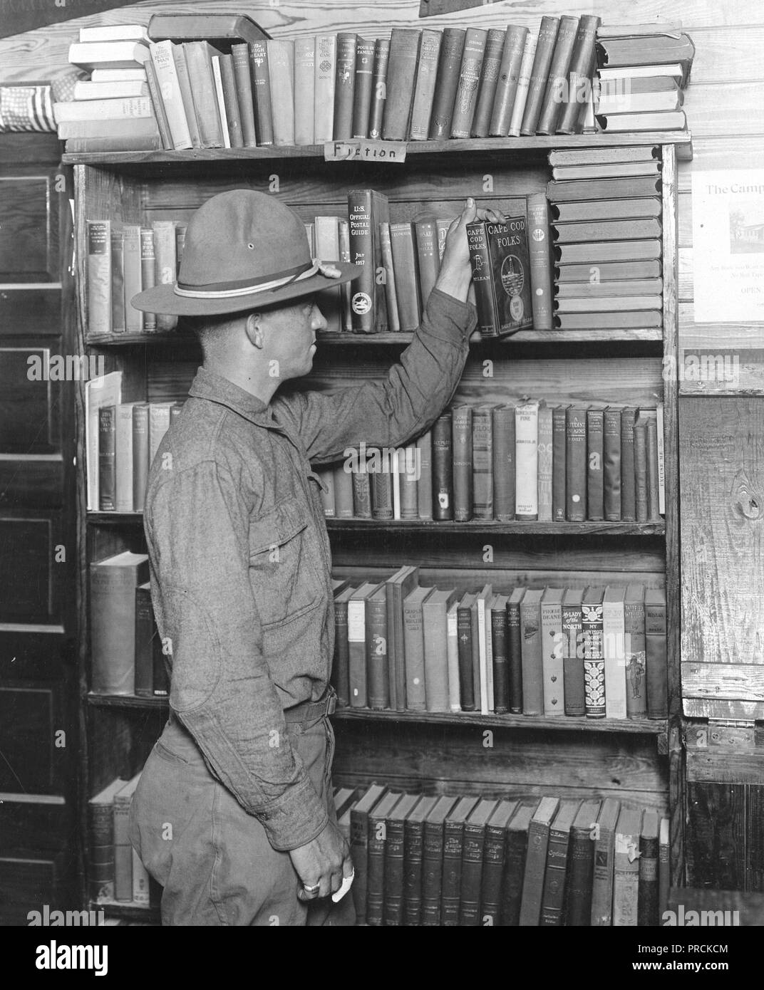 World War I era soldier looking at books on a shelf in a camp library ...