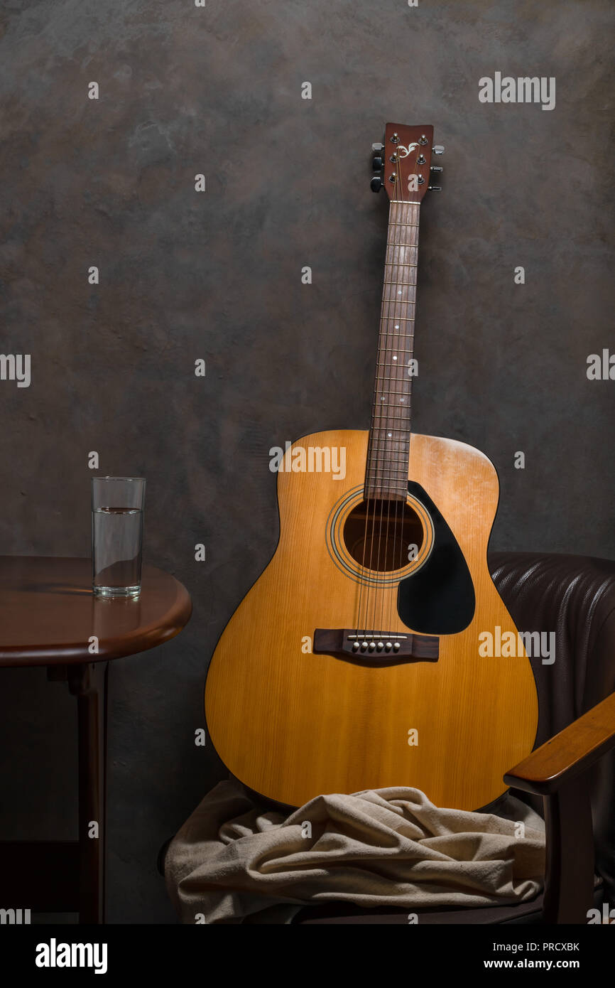 An acoustic guitar lean against the cement texture wall with a glass of ...