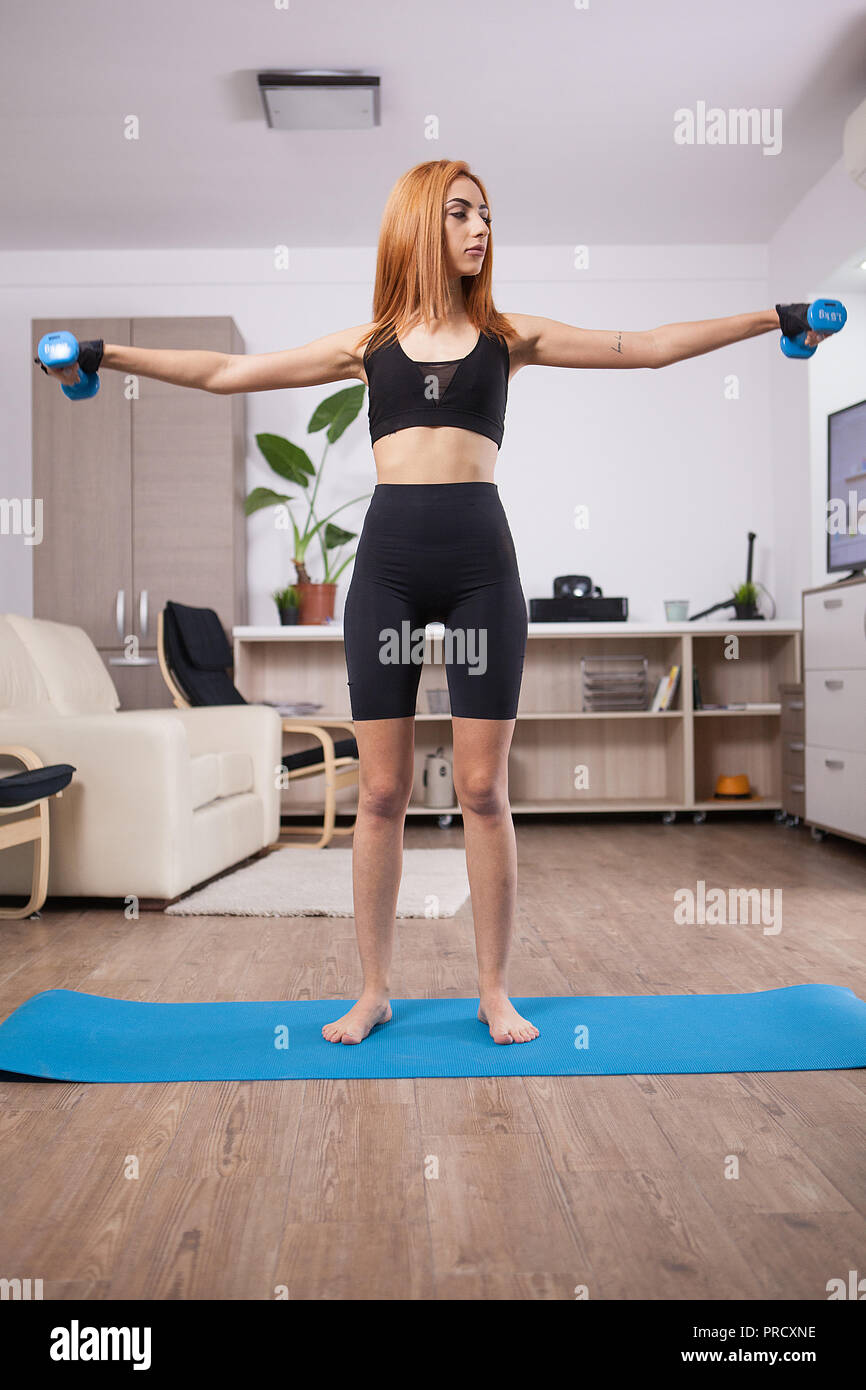 Fit girl doing lateral shoulder rises in her home training progam ...