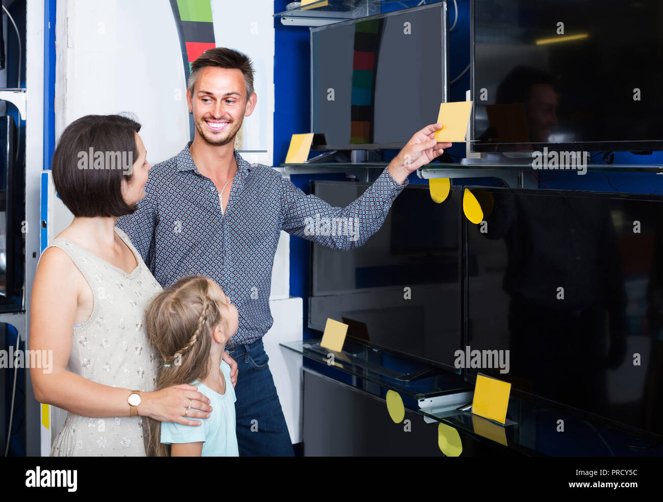 Smiling parents with daughter choosing new big TV screen in home ...