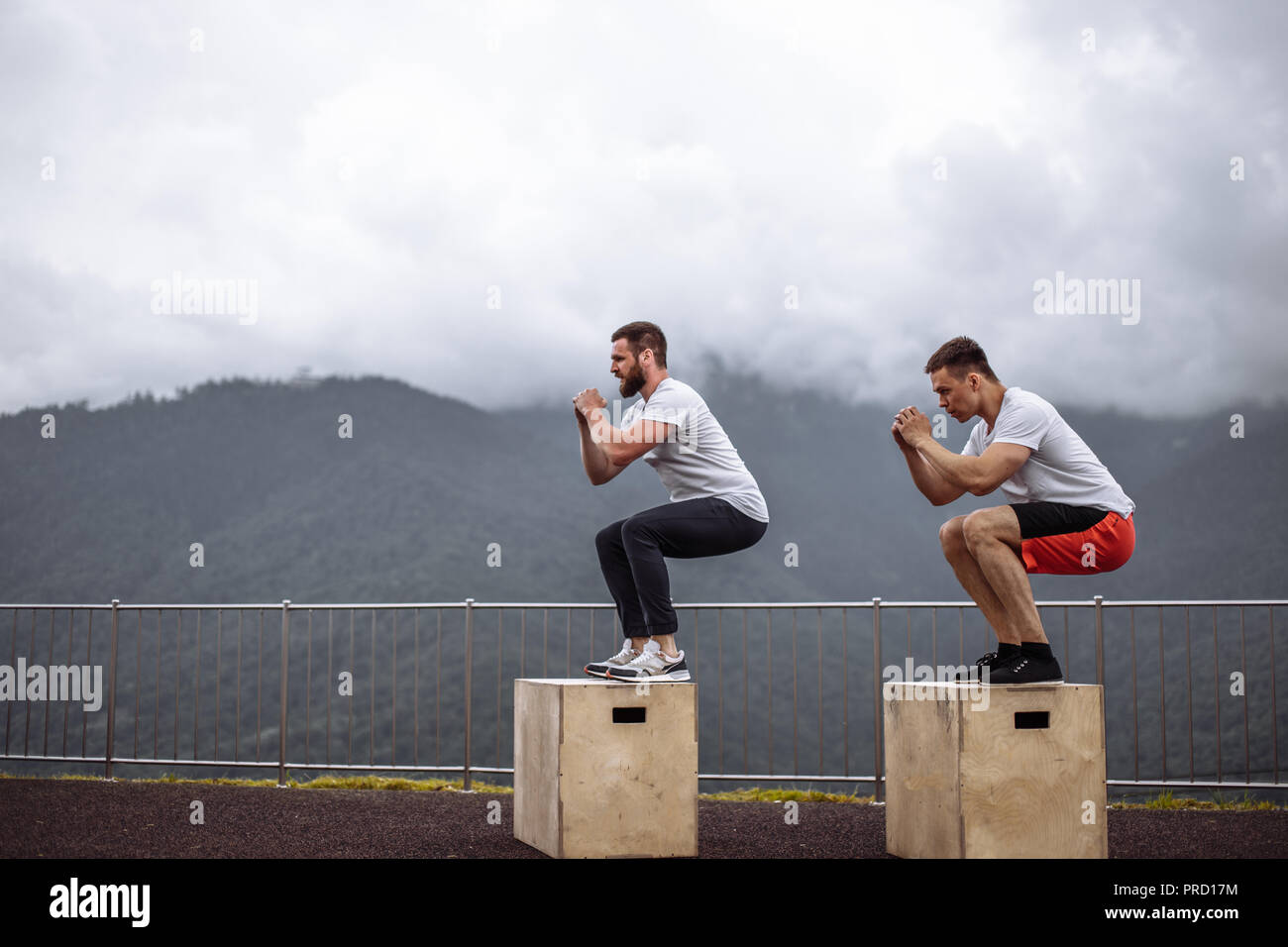 Two male athletic friends doing box jump outdoor on top of the mountain ...