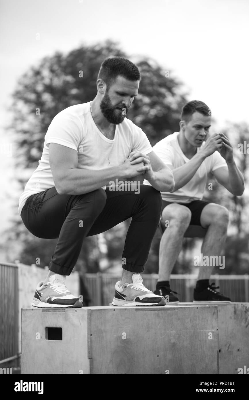 Caucasian male athletic friends doing box jump outdoor on top of the ...