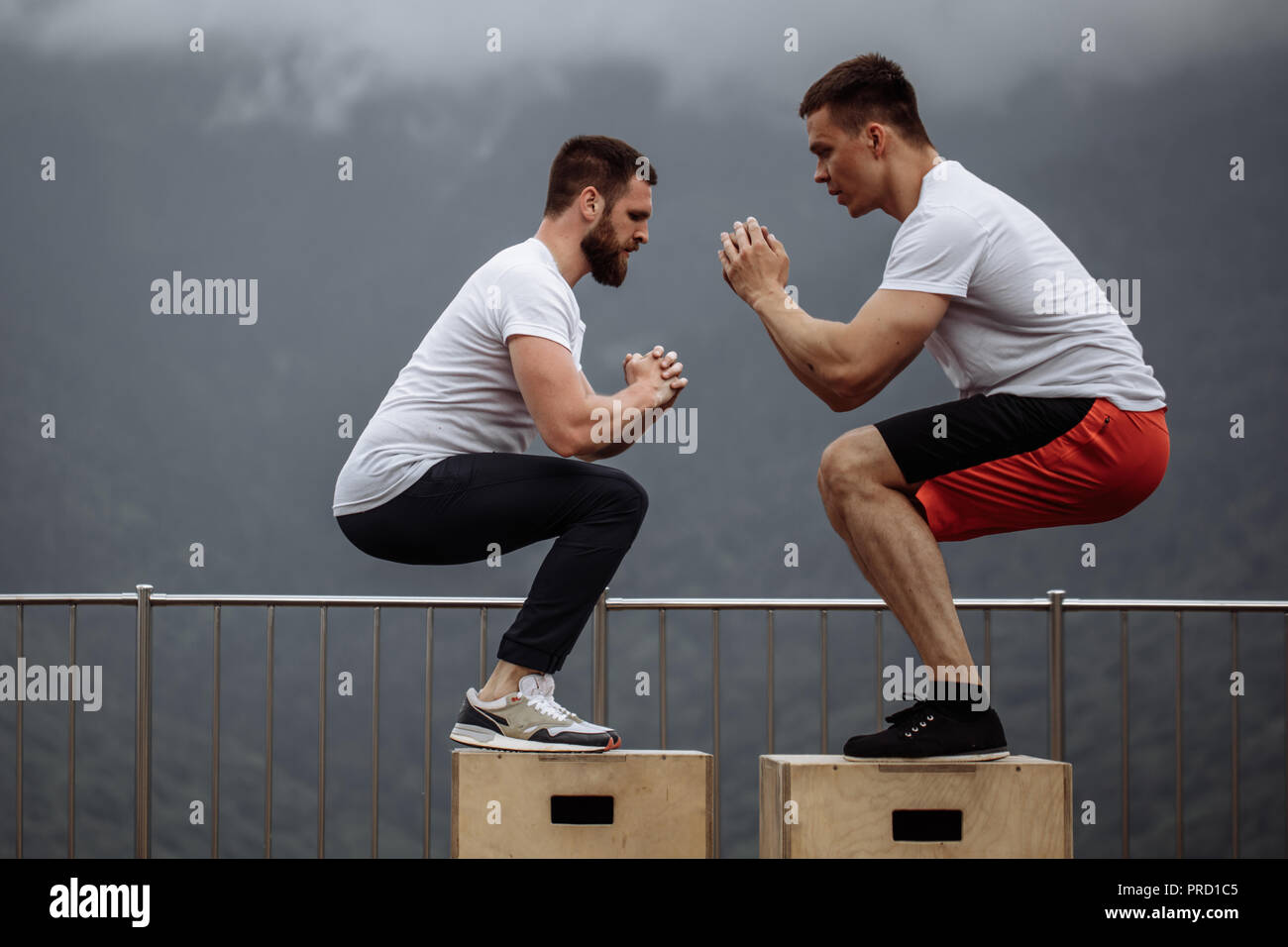 Two male athletic friends doing box jump outdoor on top of the mountain ...