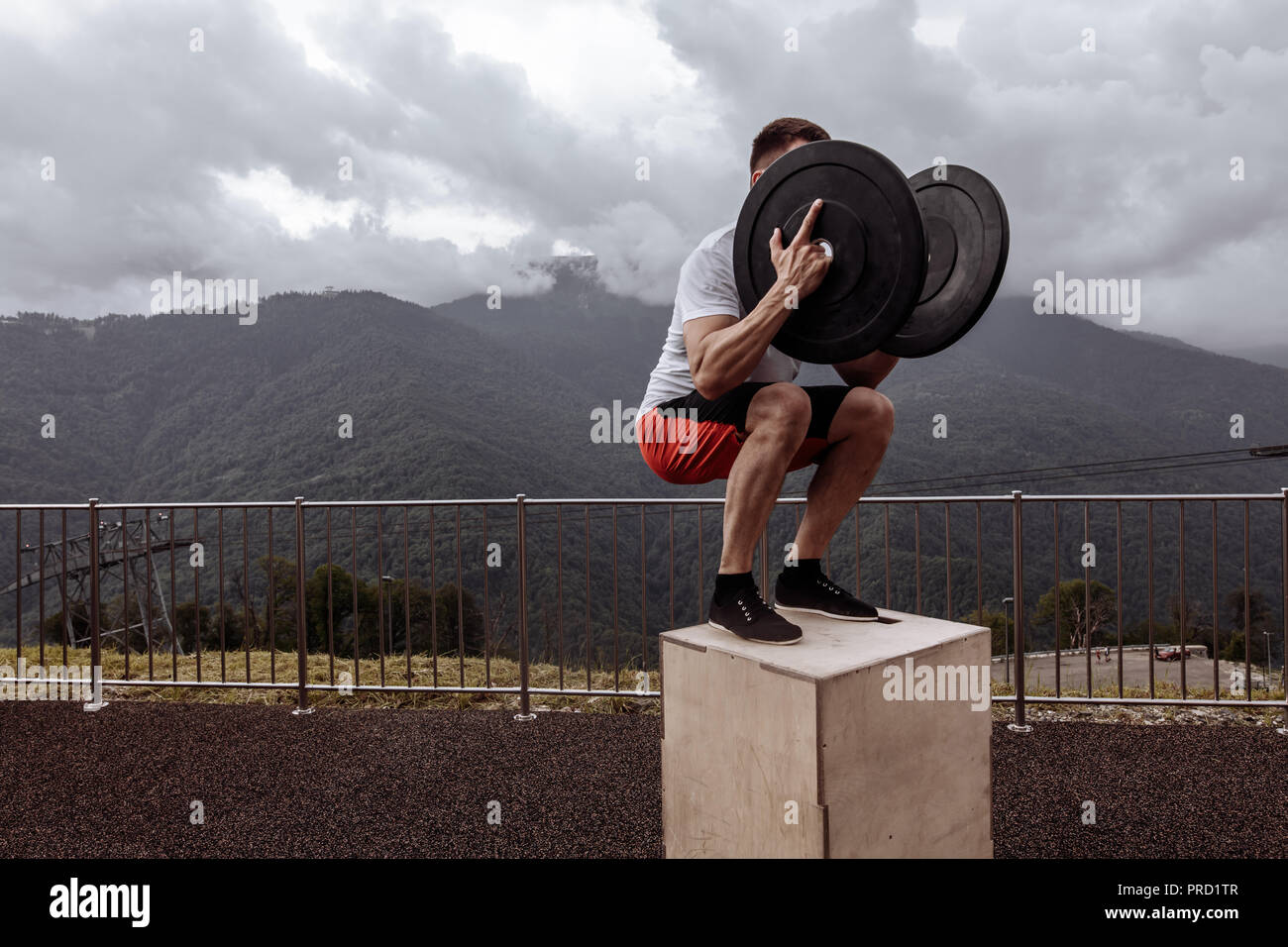 Strong male athlete doing box jumps with two plates outdoor on top of ...