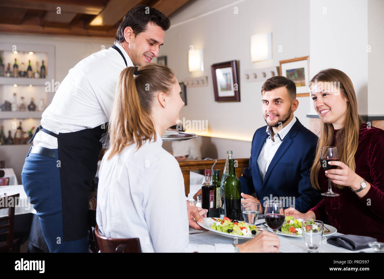 Polite smiling waiter bringing ordered dishes to guests at restaurant ...
