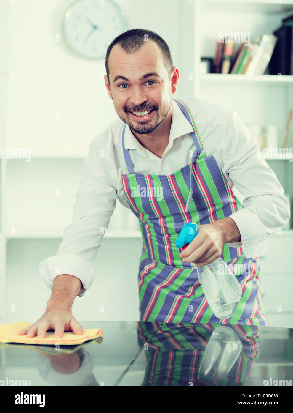 Positive young man in apron cleaning his office desk by cleanser Stock ...