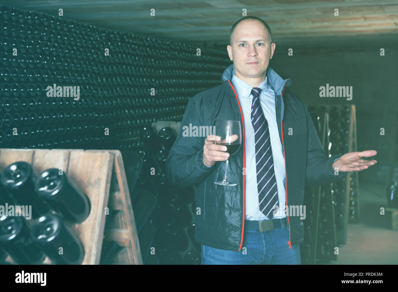 Male winemaker giving tour around winery, inviting to tasting red wine ...