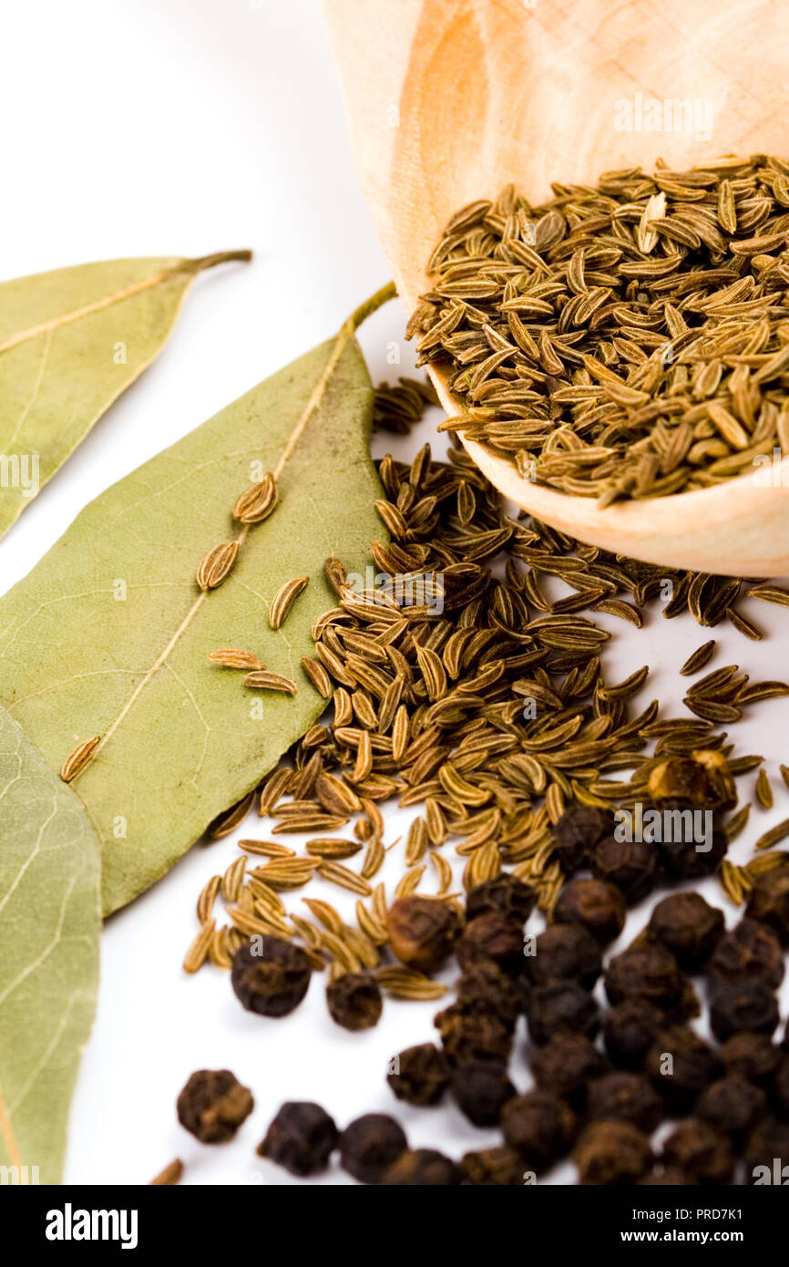 cumin on wooden spoon, black pepper, and bay leaves on white background ...