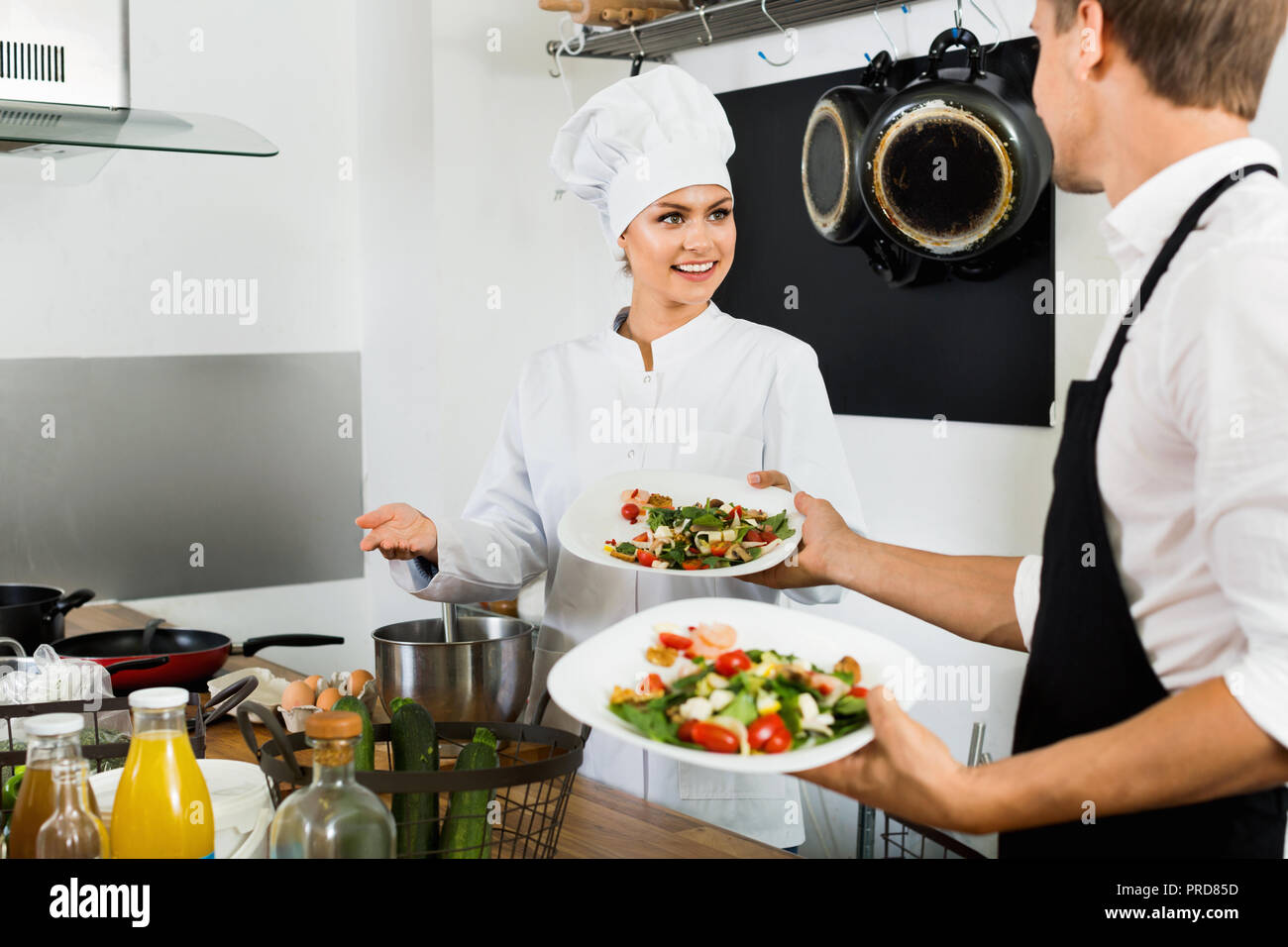 Portrait of young smiling woman cook giving to waitress ready to serve ...