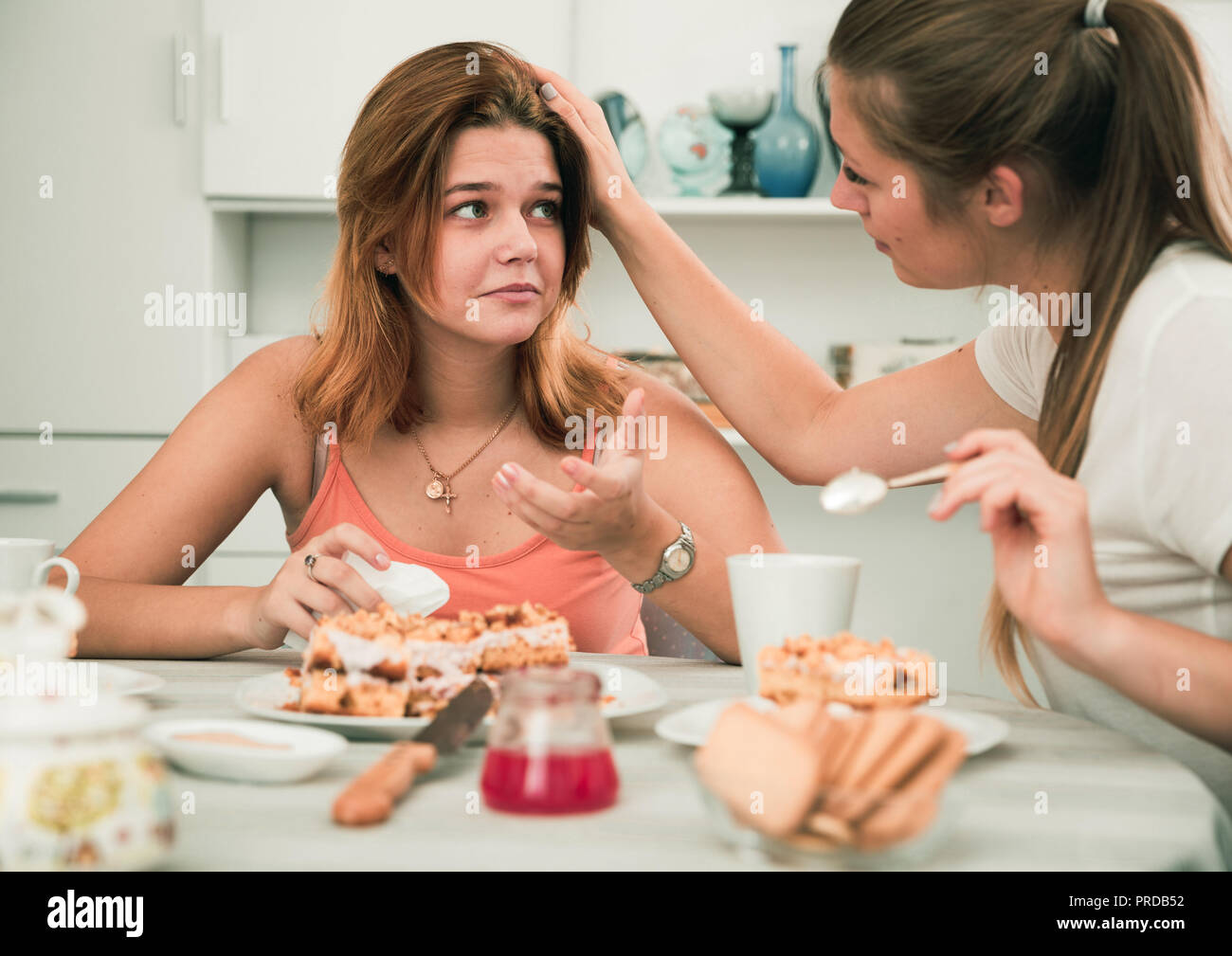 Female talking with young sad friend at the table with cake at home ...