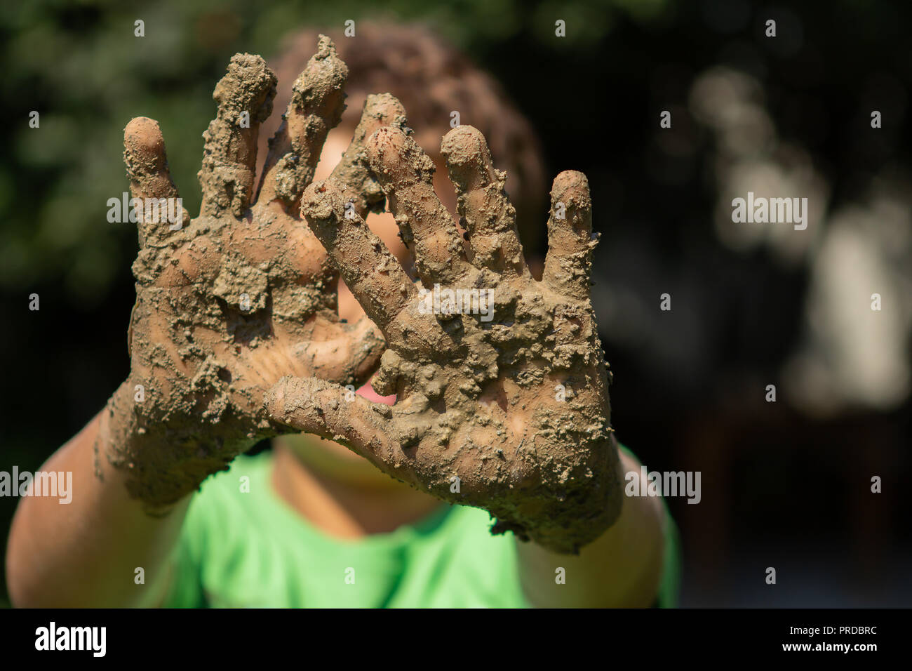 A cute little boy kid is plays outside in the mud. Child is showing his ...