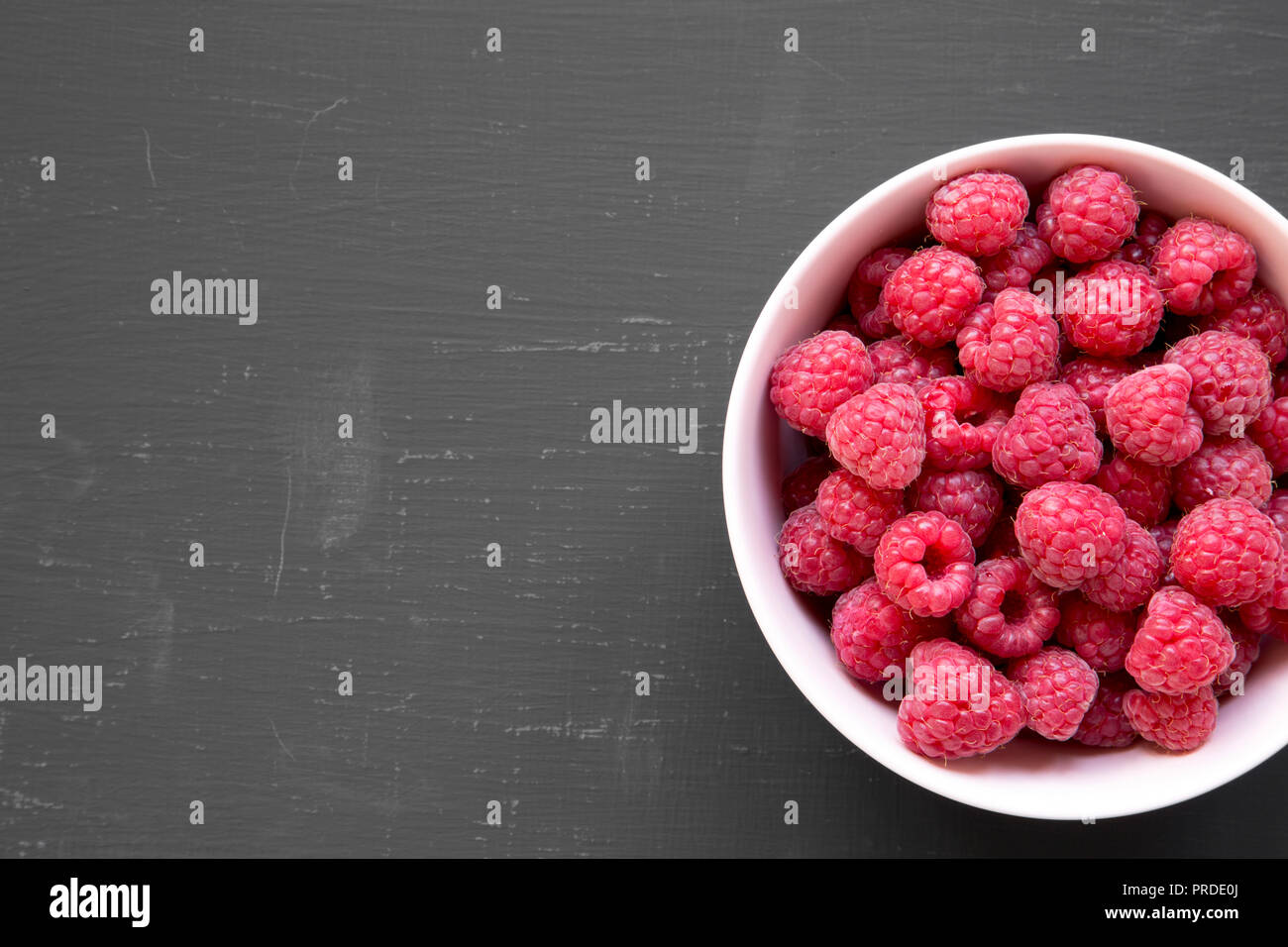 Pink bowl of raspberry on black background, overhead view. From above ...