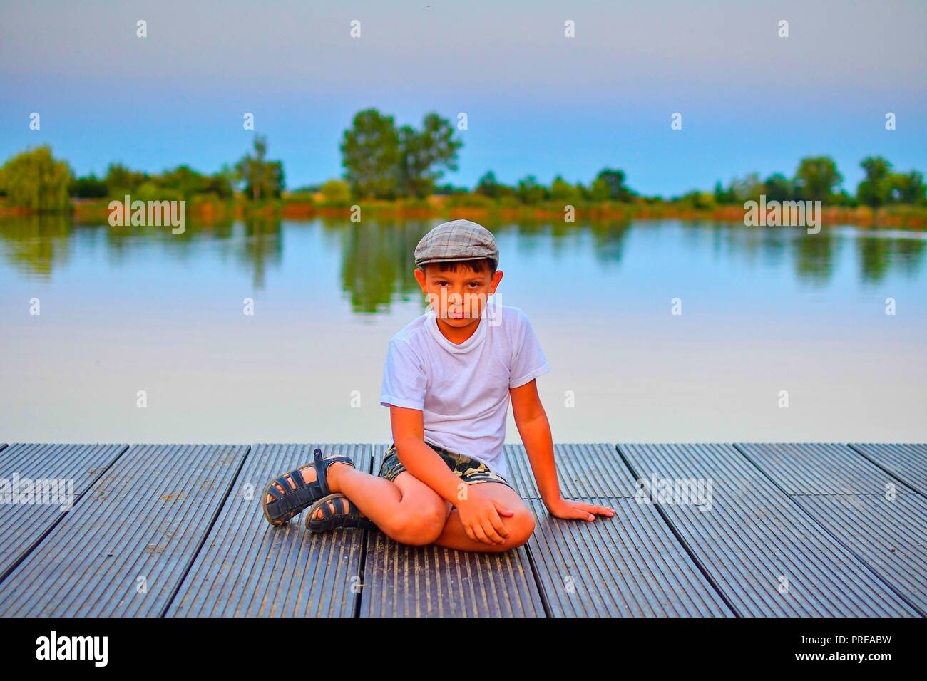Little boy sitting on pier. Elementary age boy sitting on a wooden pier ...
