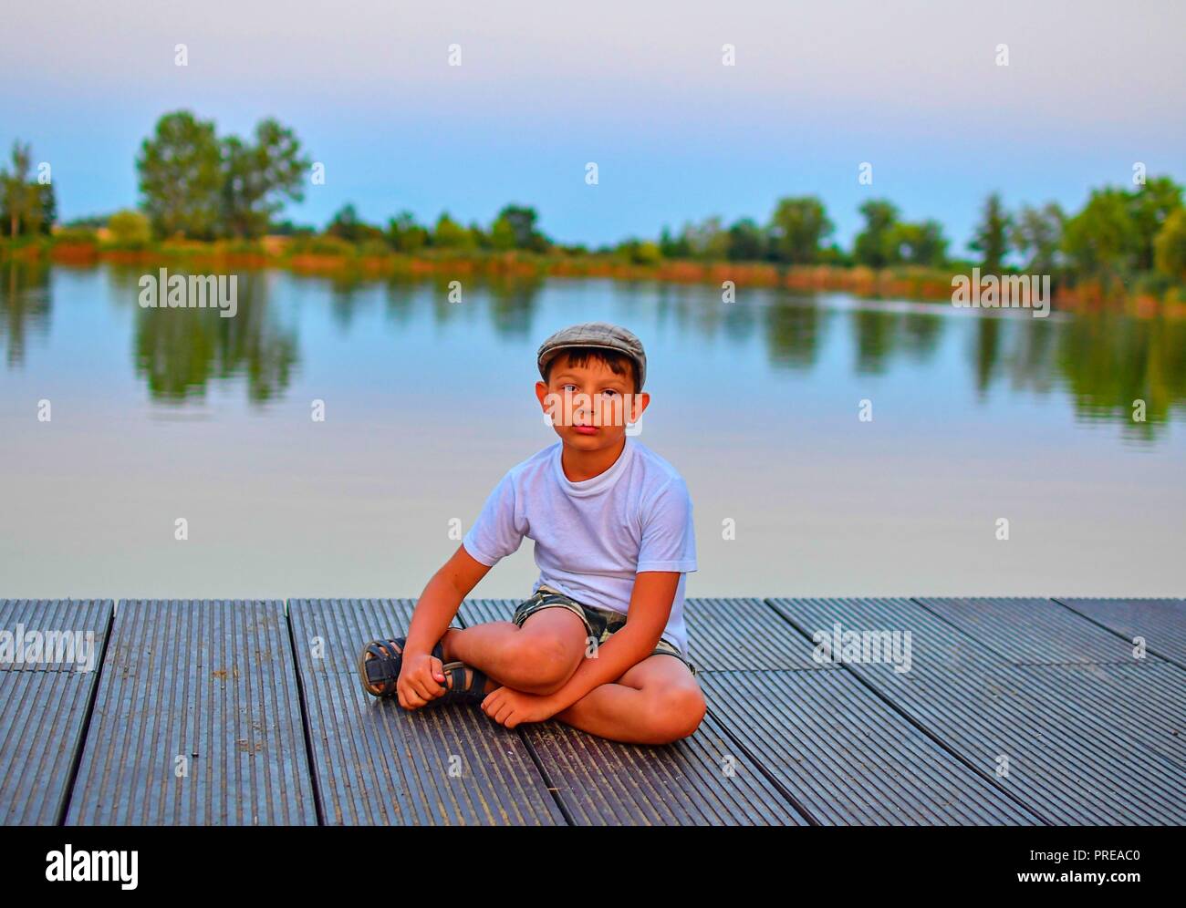 Little boy sitting on pier. Elementary age boy sitting on a wooden pier ...