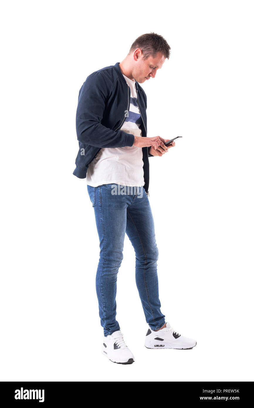 Side view of young casual man typing message on mobile phone. Full body ...