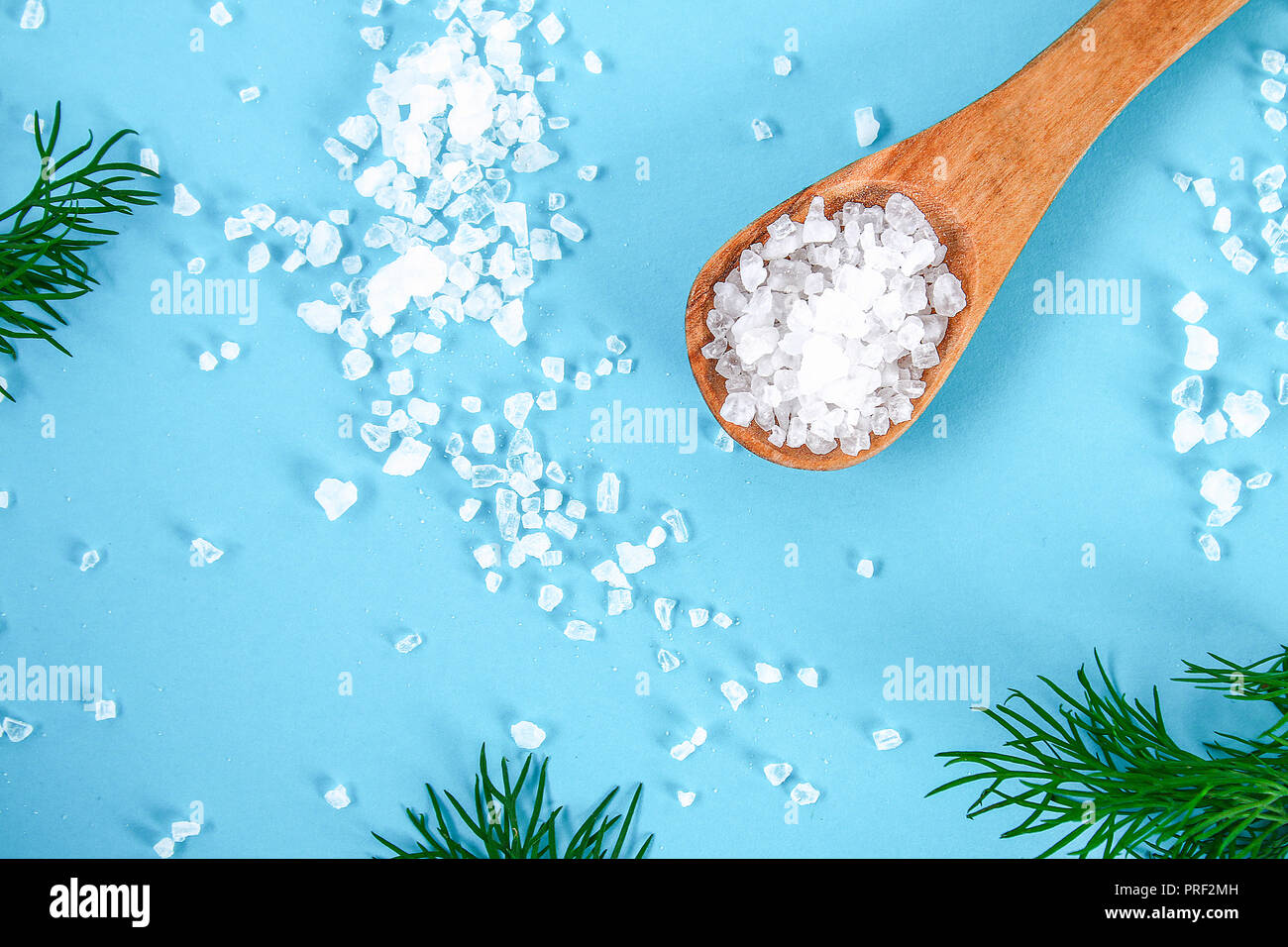 Crystals of large sea salt in a wooden spoon and dill on a blue table ...