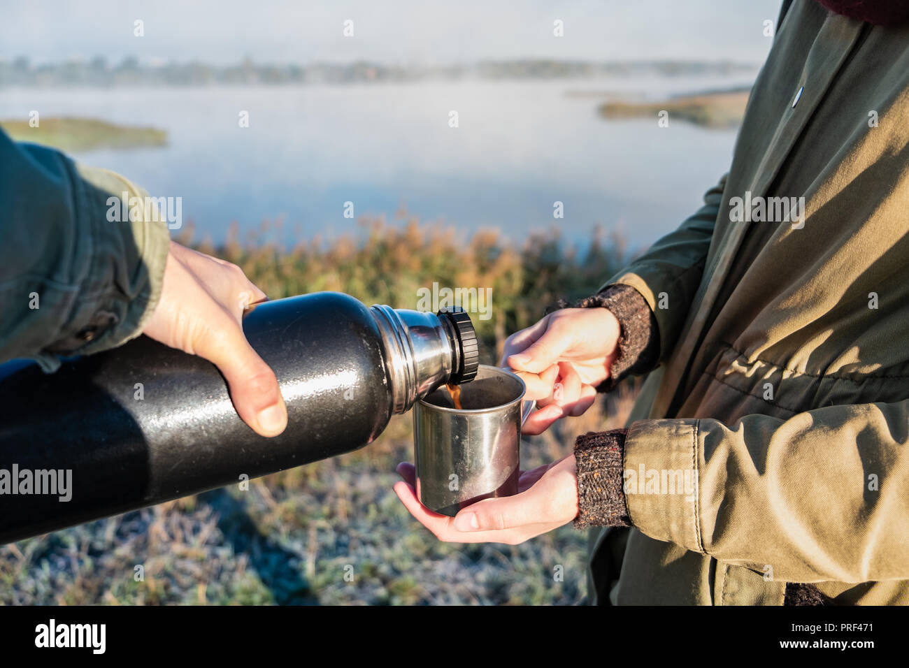 Pouring hot coffee out of thermos flask at beautiful riverbank. Two ...