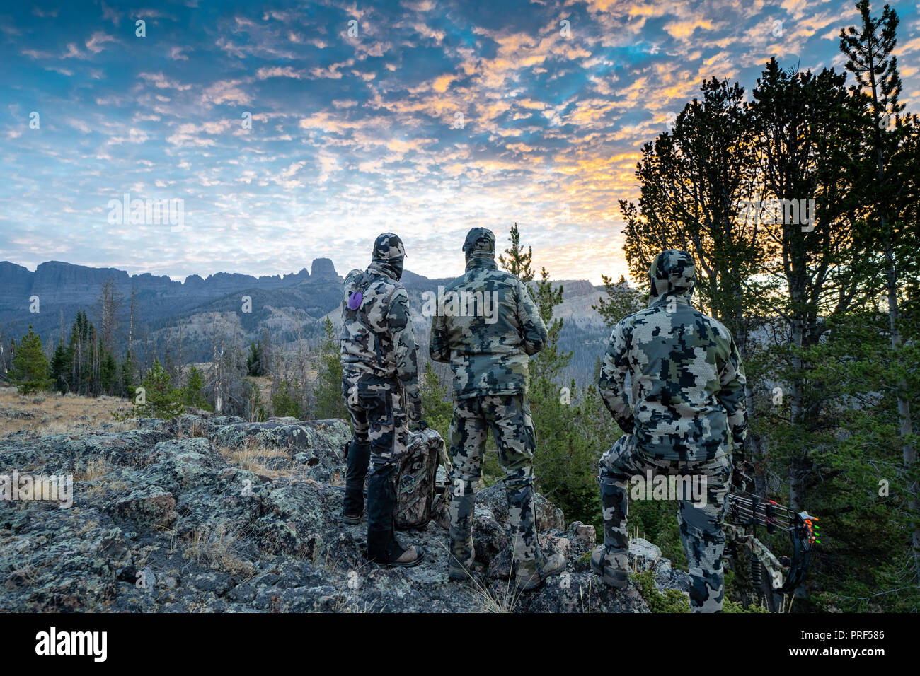Three adult male hunter friends, unrecognizable, stand on a mountain ...