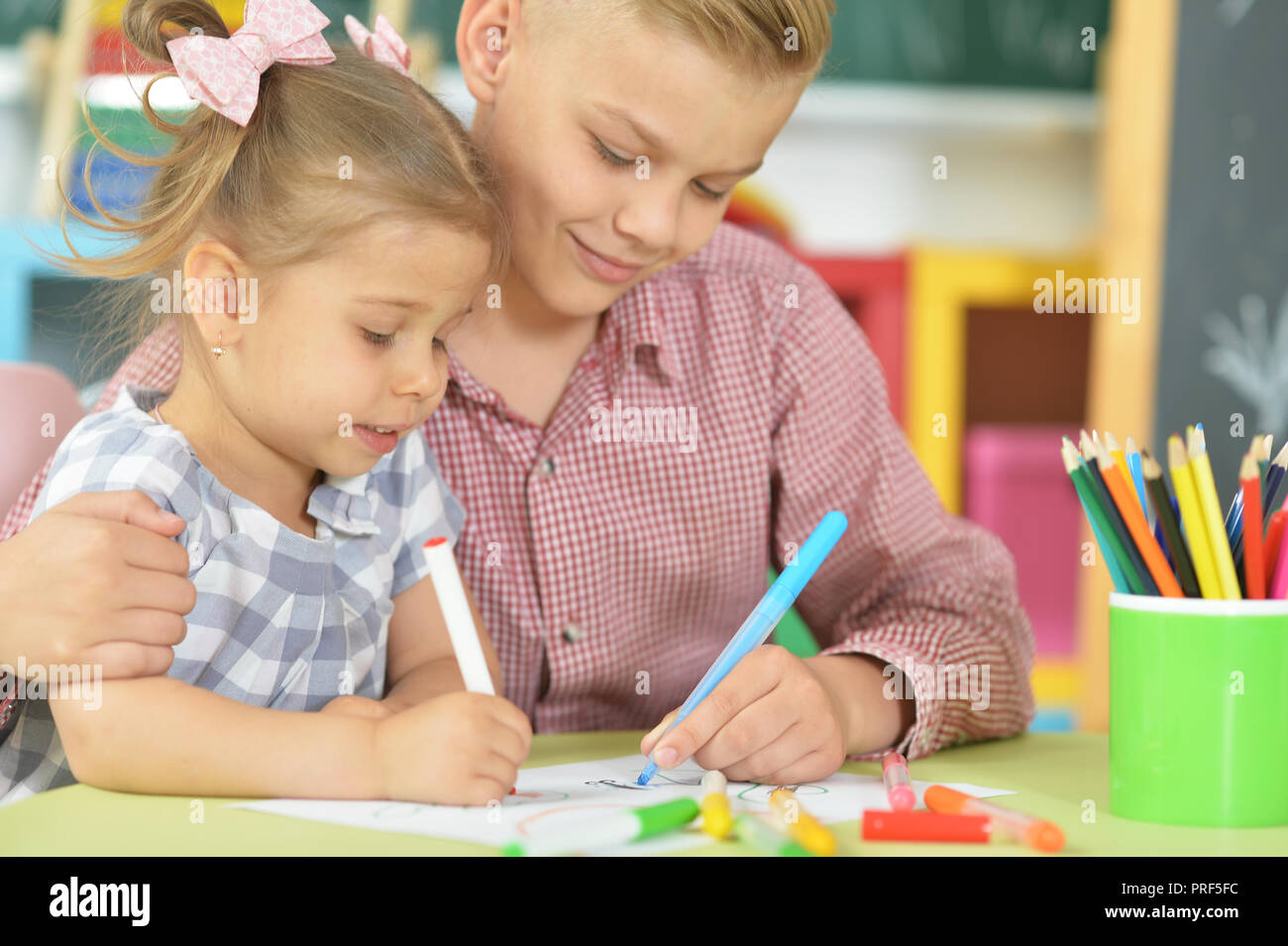 Smiling brother and sister drawing with felt pens together indoors ...