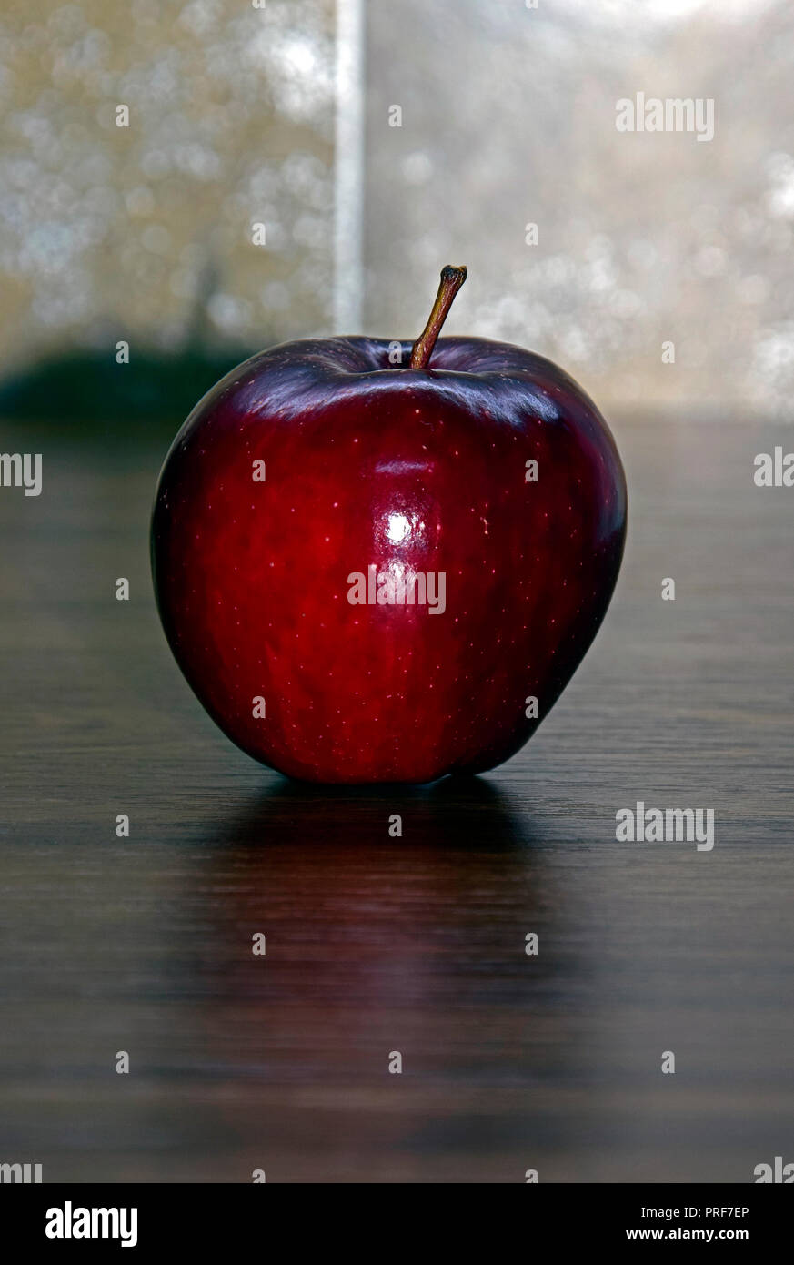 A ripe, shiny red apple, on brown wooden desktop and with abstract ...