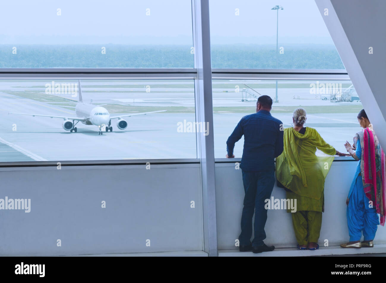 Family looking thru the window at plane in airport. Spending time until ...