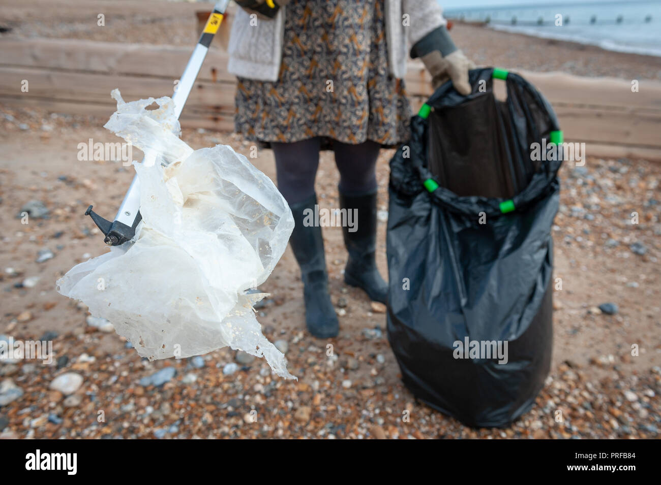 A woman picks up plastic waste using a litter picker from the beach ...