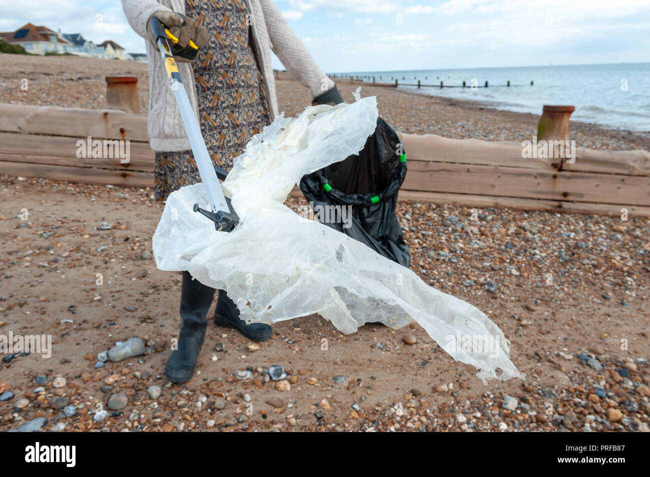 A woman picks up plastic waste using a litter picker from the beach ...