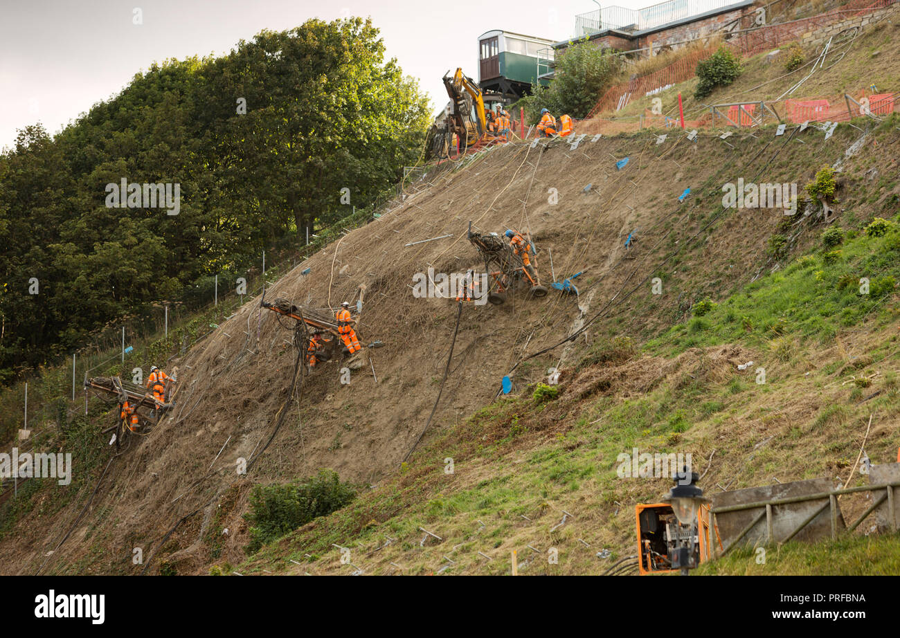 Engineers in harnesses fixed by long cables work on a cliff face at ...