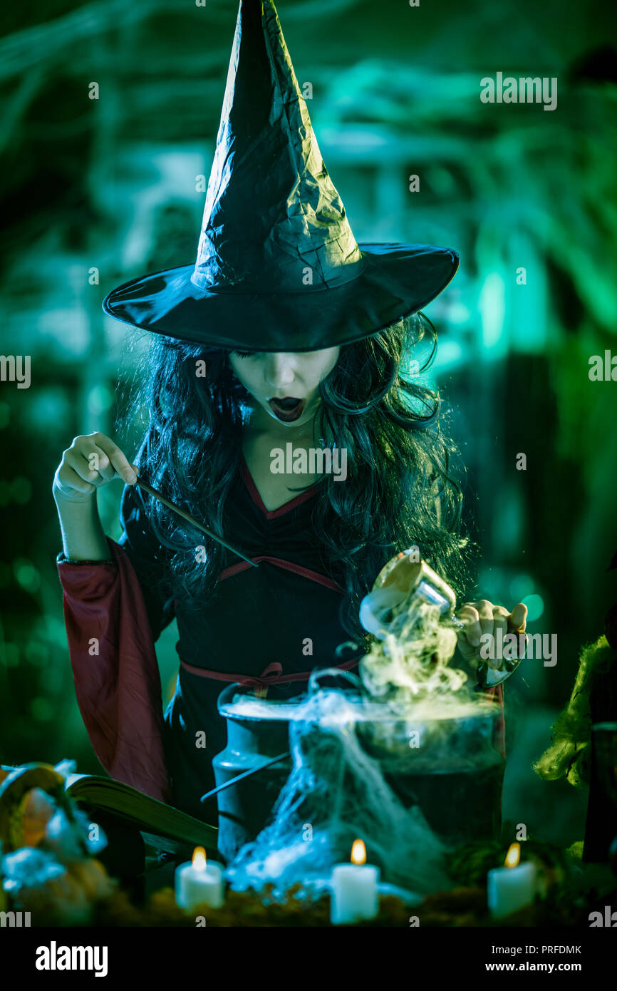 Young witch with angry evil face holds a goblet with magic potion in ...