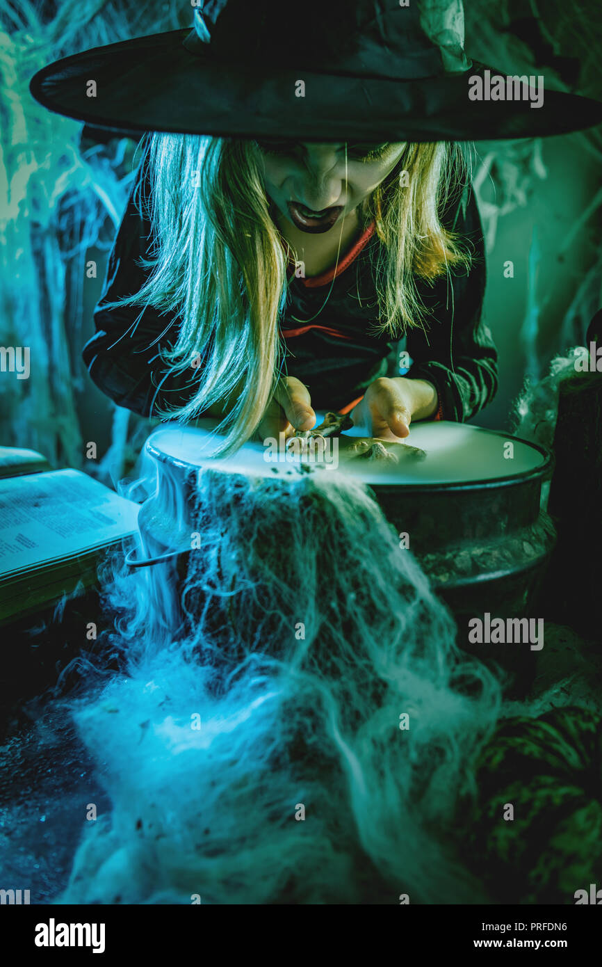 Young angry witch with awfully face tells evil words, and putting bones ...