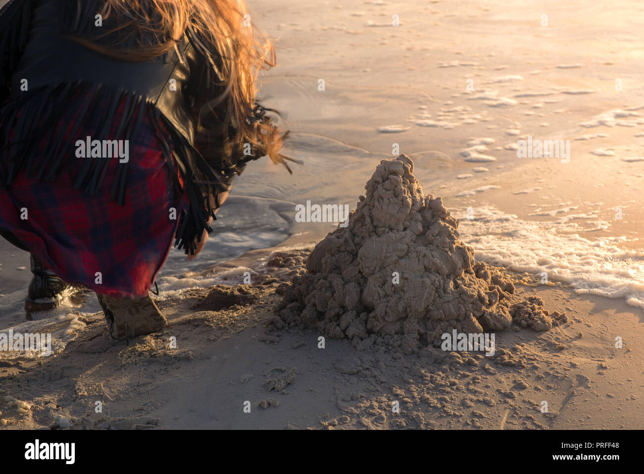Young woman building and making sand castle next to sea. Calm, relaxing ...