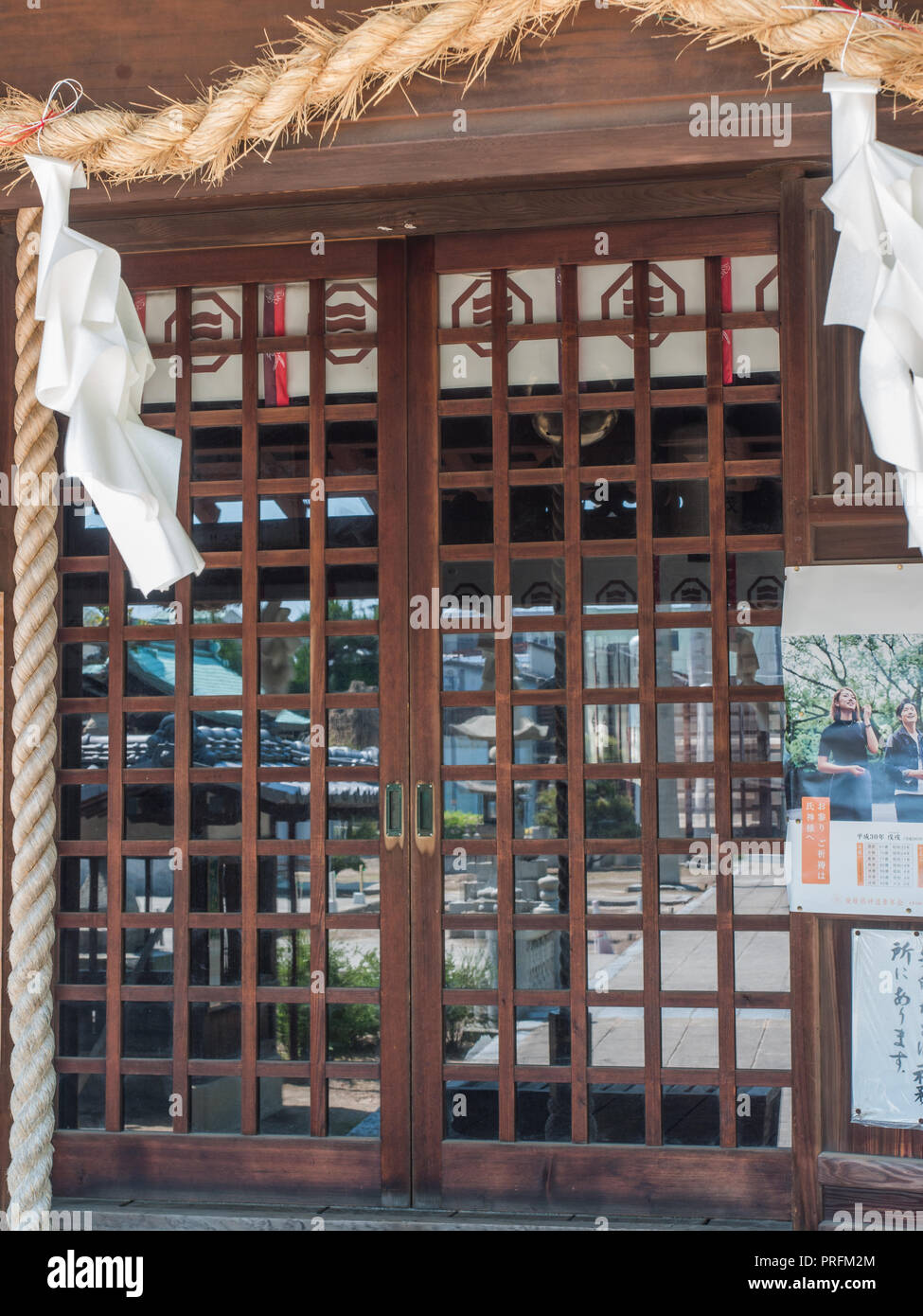 Reflections in glass sliding door, a shinto shrine, shimenawa rope and ...