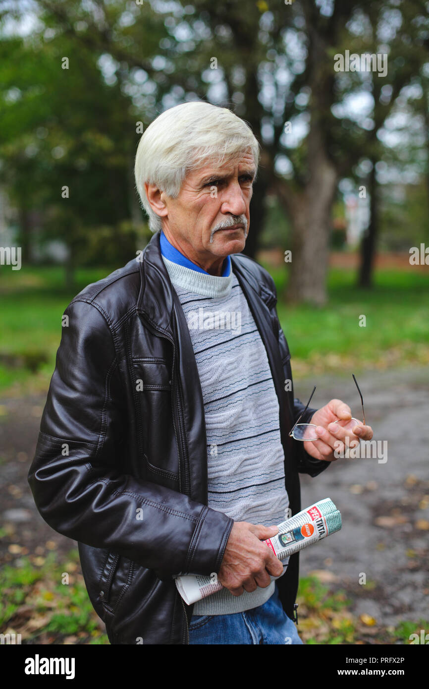 a portrait of a gray man is 60 years old. He holds a newspaper in his ...