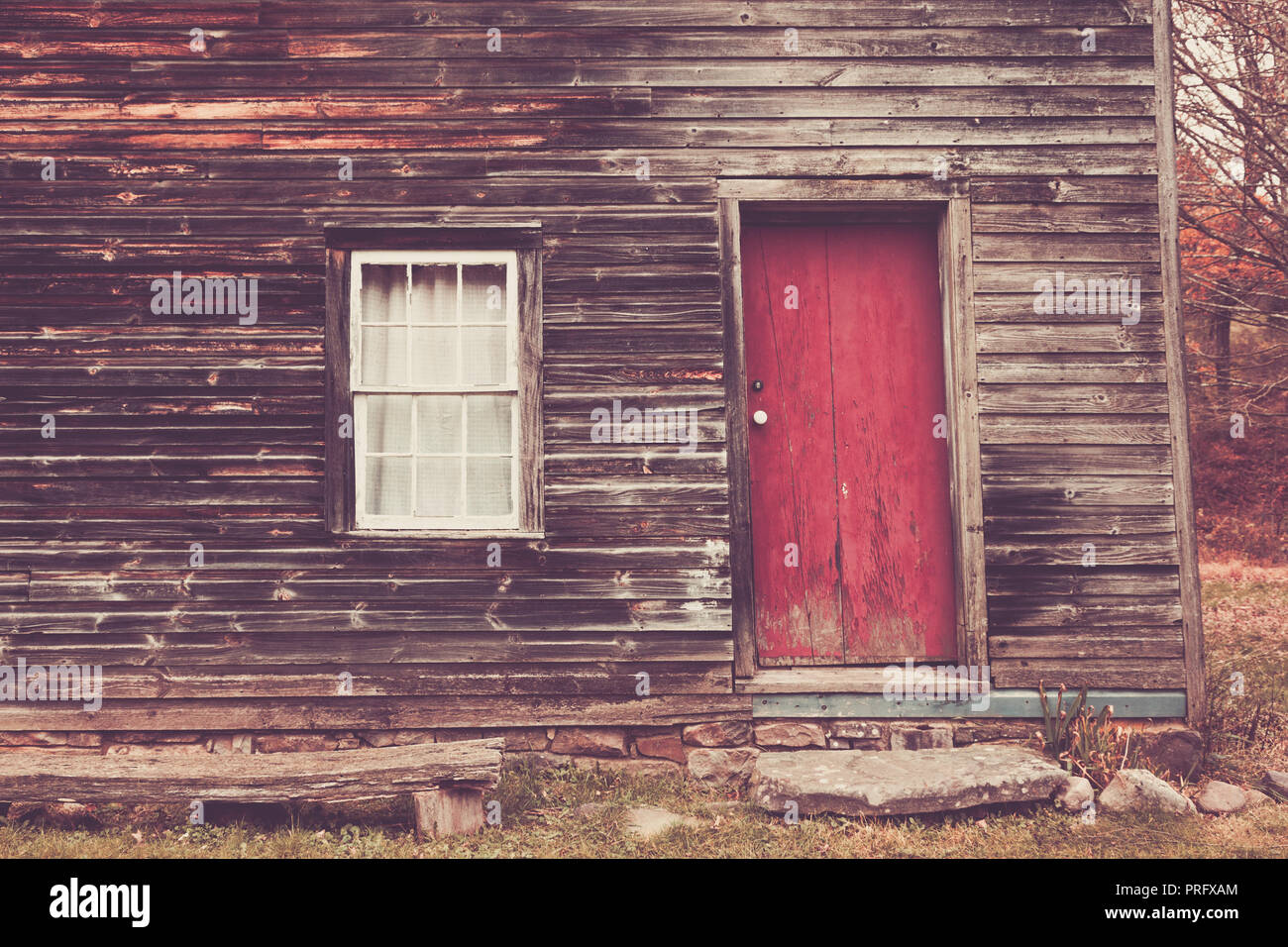 An old red door serves as an entrance to a plain sided wooden house ...