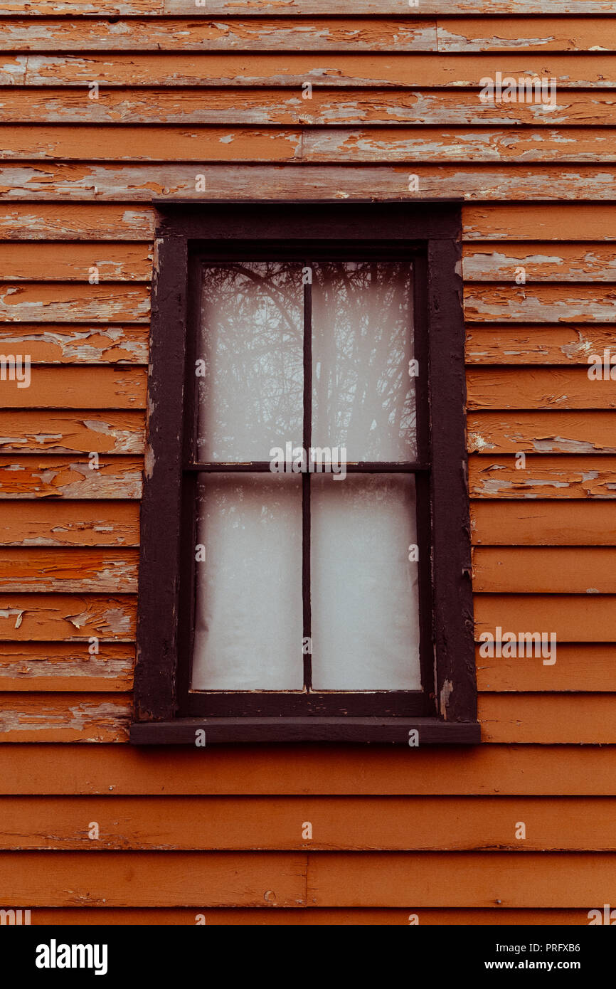 An old paned glass window is surrounded by peeling paint on wooden ...