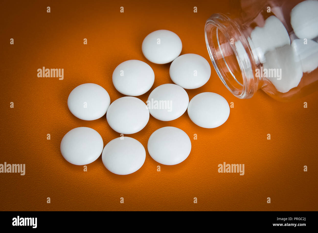 White tablets are scattered from a glass bottle on a yellow background ...