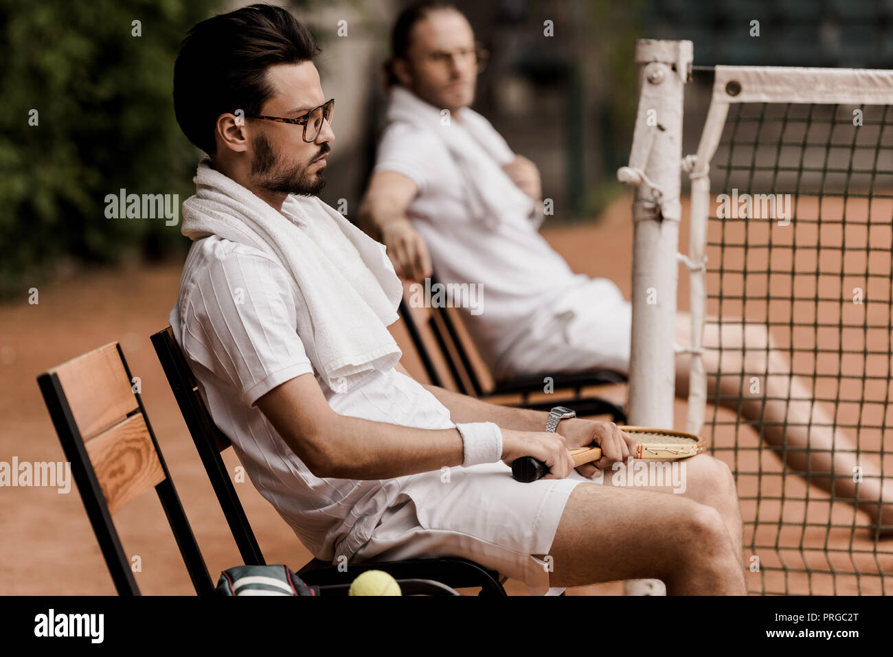 side view of retro styled tennis players resting on chairs with towels ...