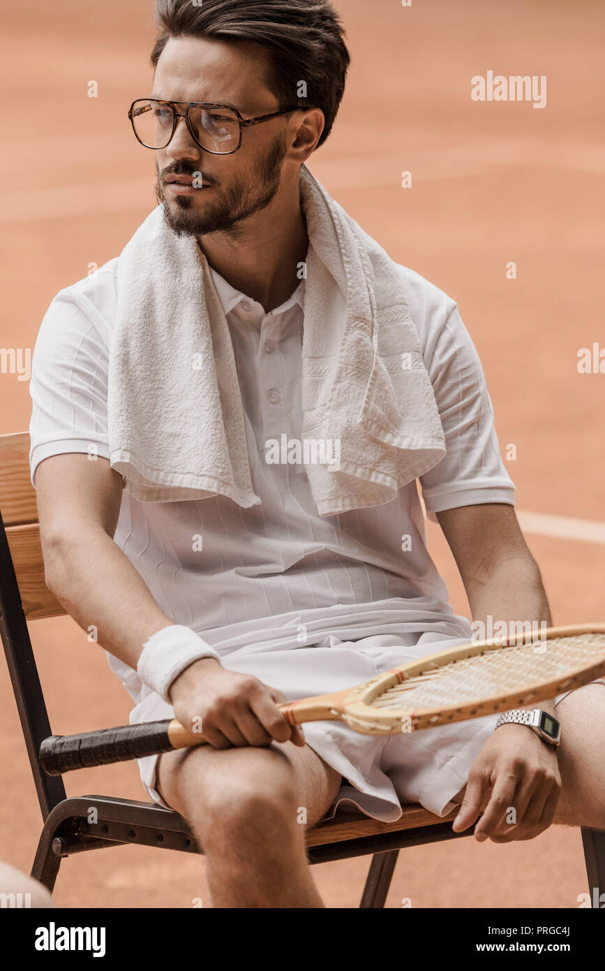 handsome tennis player sitting on chair with tennis racket at court ...