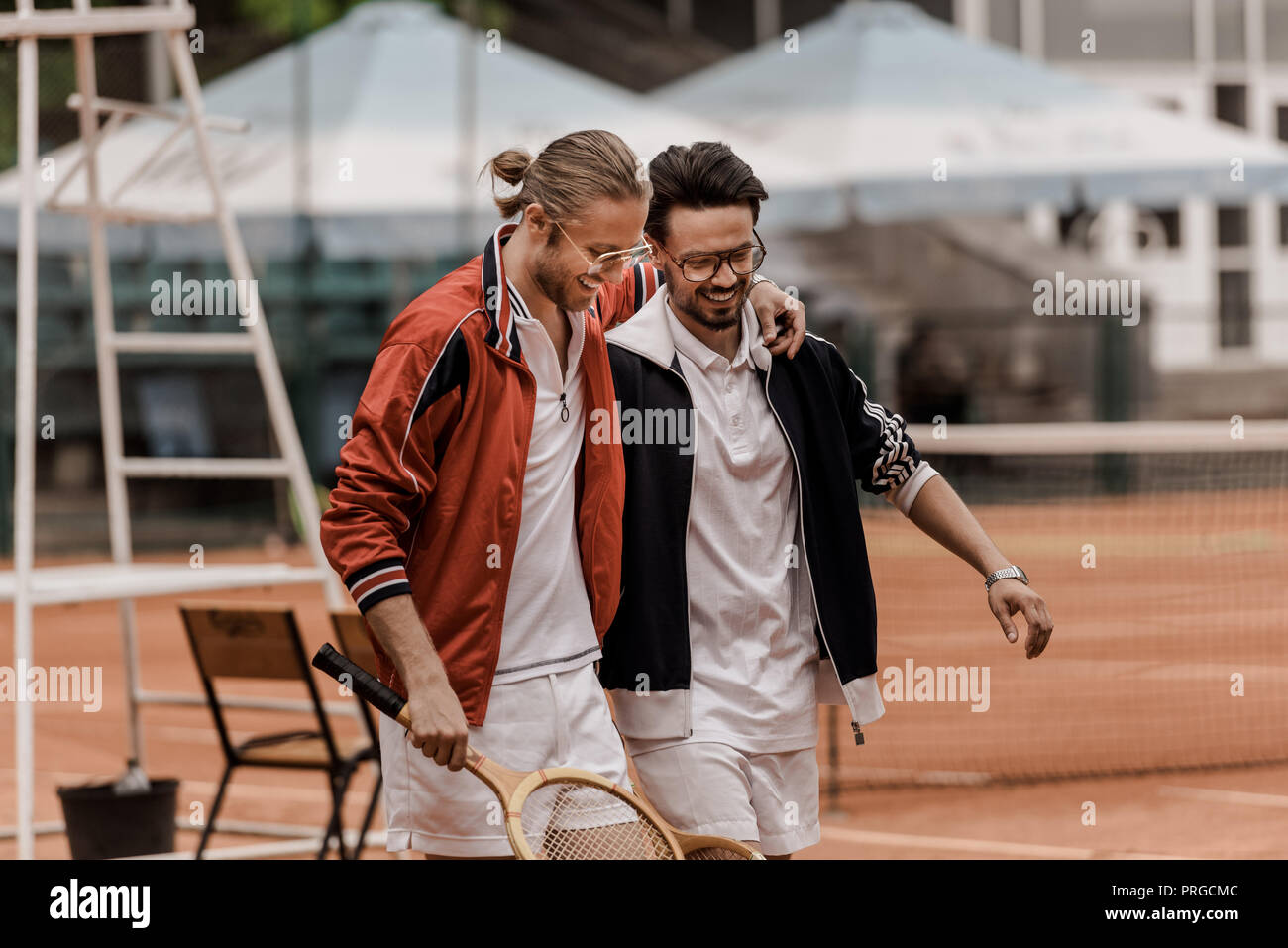 smiling retro styled tennis players walking with rackets and hugging at ...