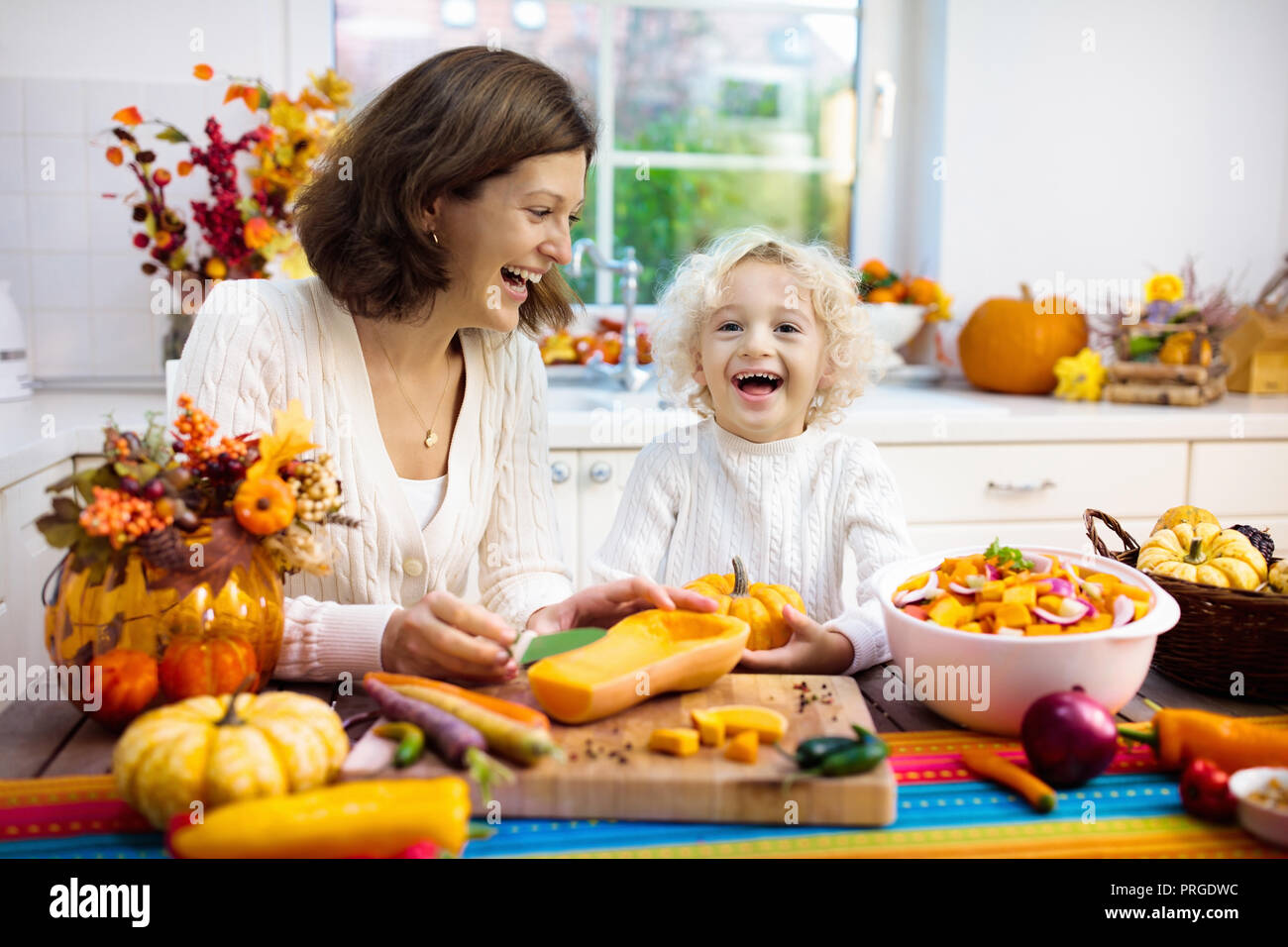 Mother and son cutting pumpkin, onion and carrot, cooking soup for ...